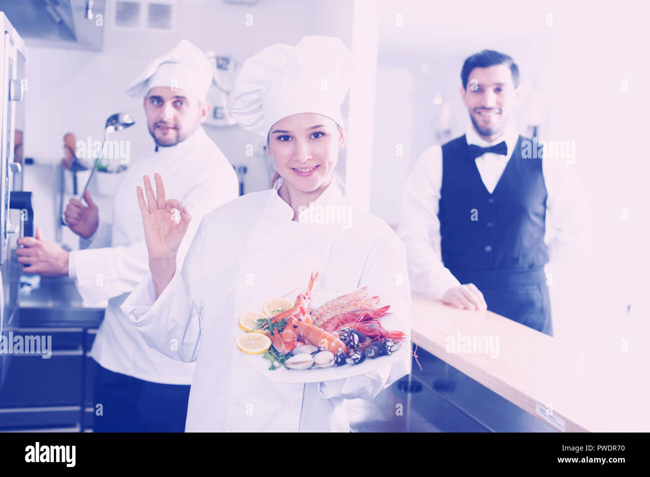 Smiling woman chef approving dish in kitchen of fish restaurant before ...