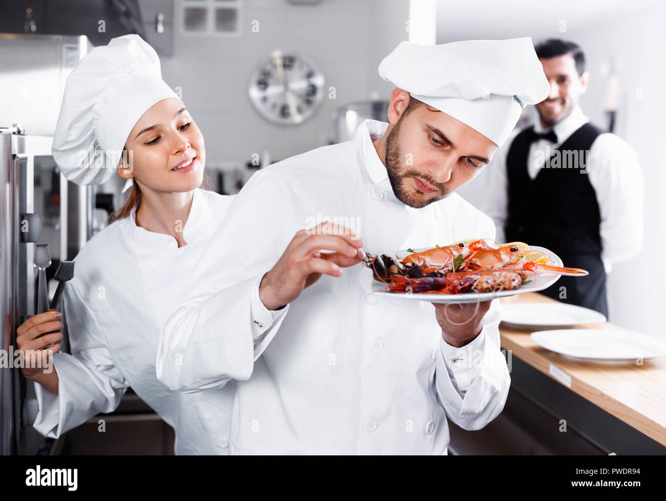 Head glad cheerful chef checking dishes in kitchen of fish restaurant ...