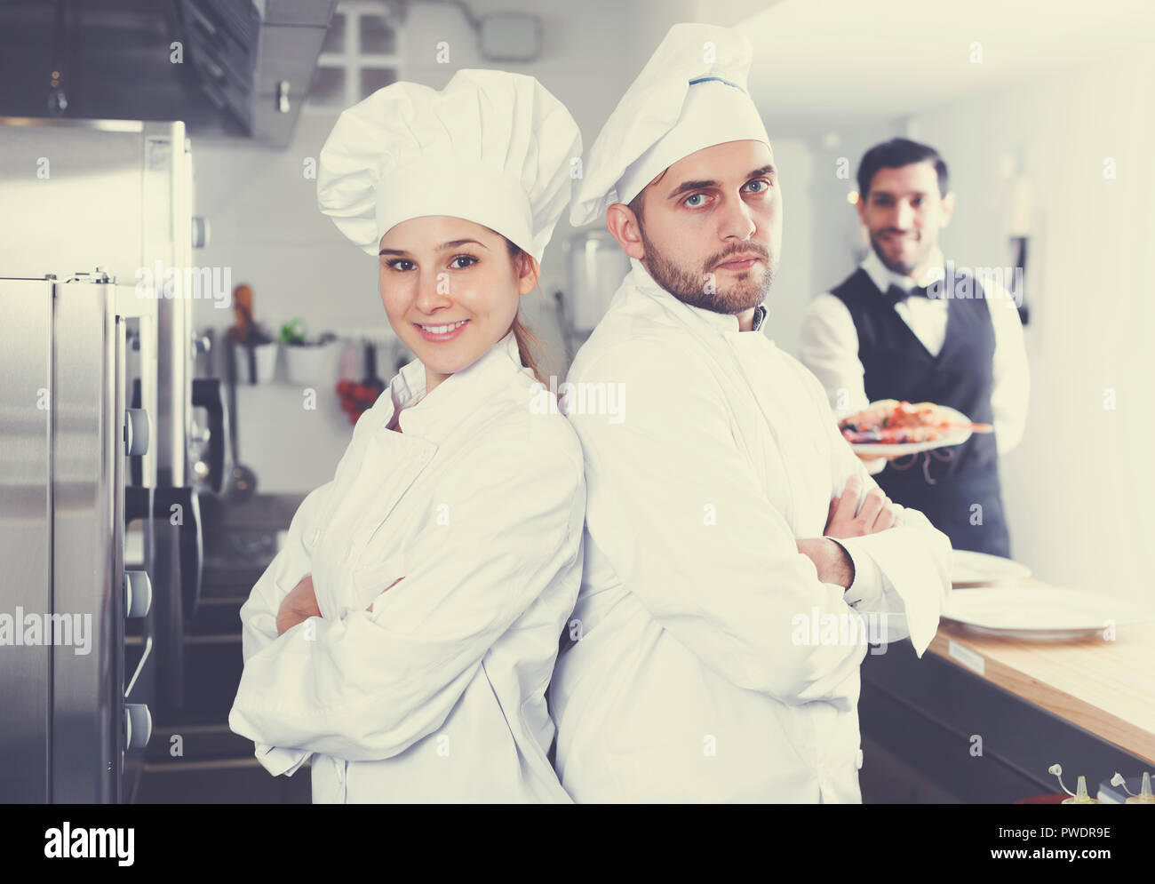 Portrait of two young confident fish restaurant chefs, standing back to ...