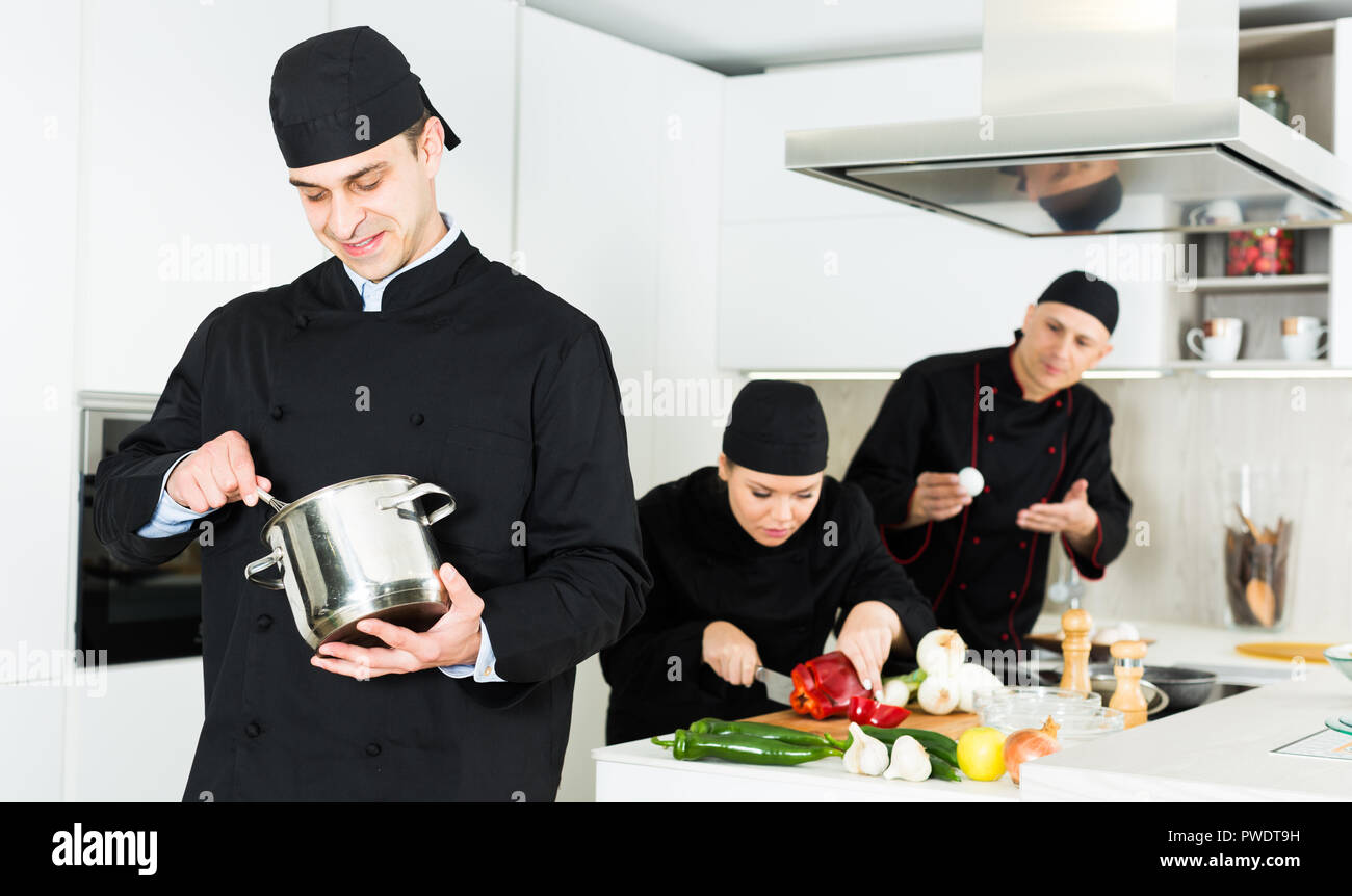 Smiling male kitchener in uniform is standing with pot in the kitchen ...