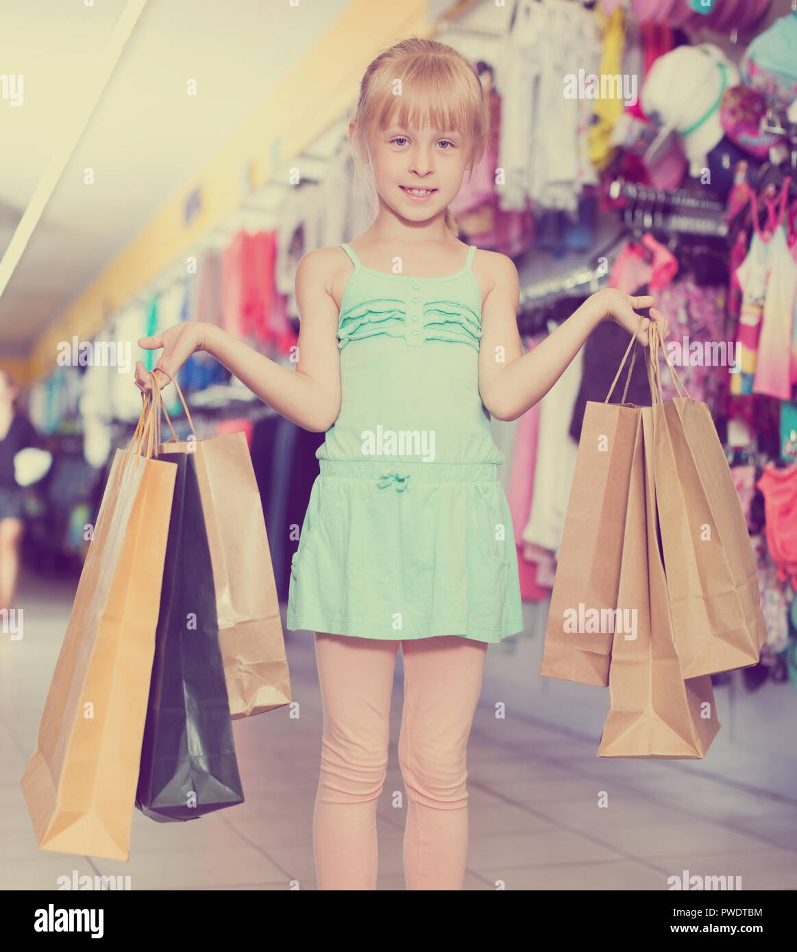 Smiling little girl holding packages with wear for children in the shop ...