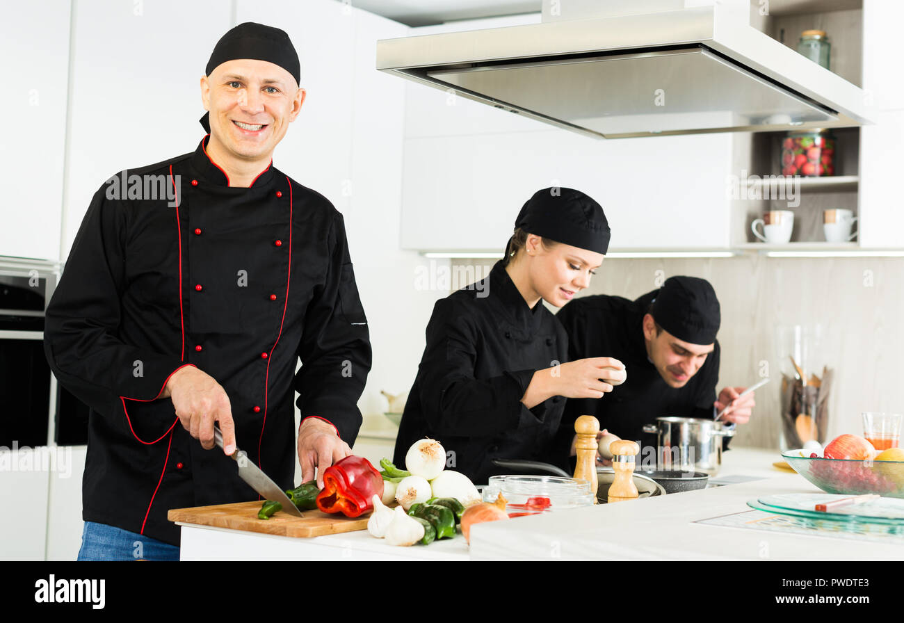 Team of woman and man chefs in black uniform preparing food on kitchen ...
