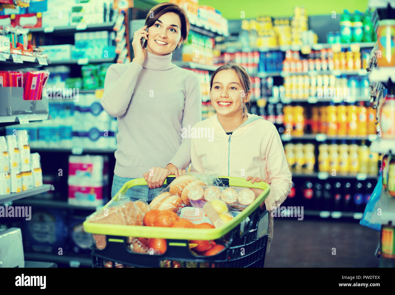 Young smiling glad female shopper talking on phone being with teenager ...