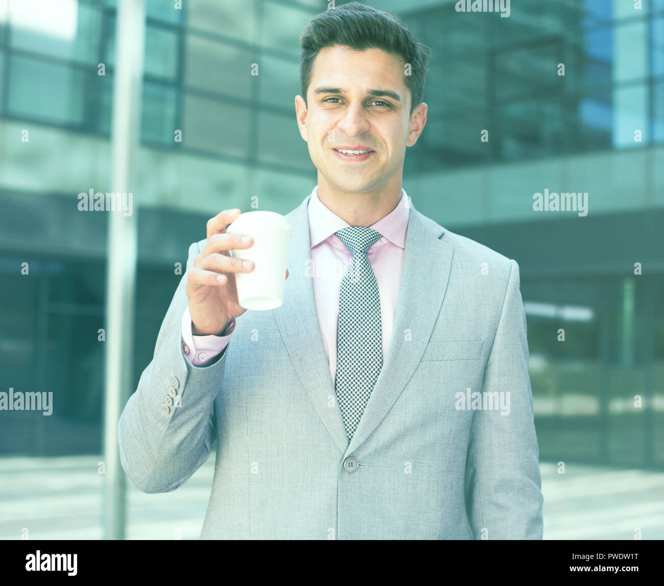 Portrait of young successful businessman drinking coffee near large ...