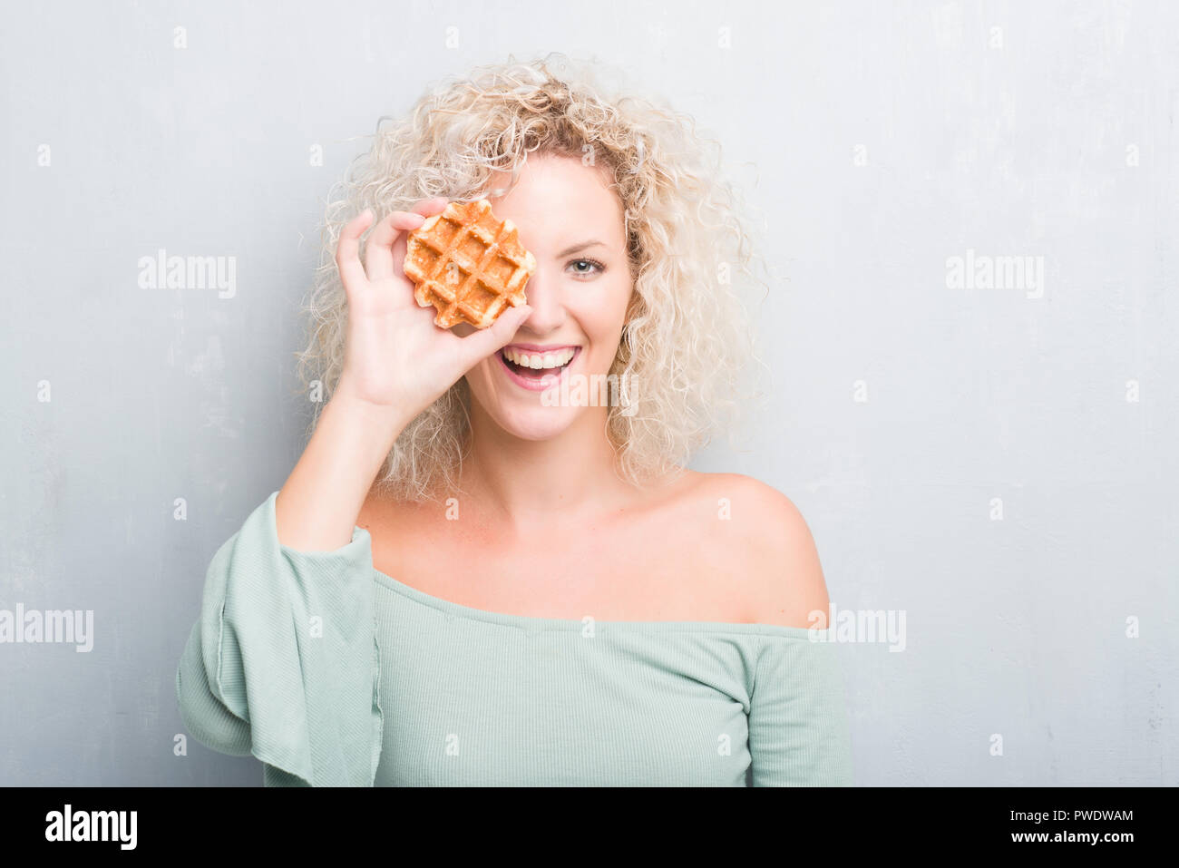 Young blonde woman over grunge grey background eating belgian waffle ...