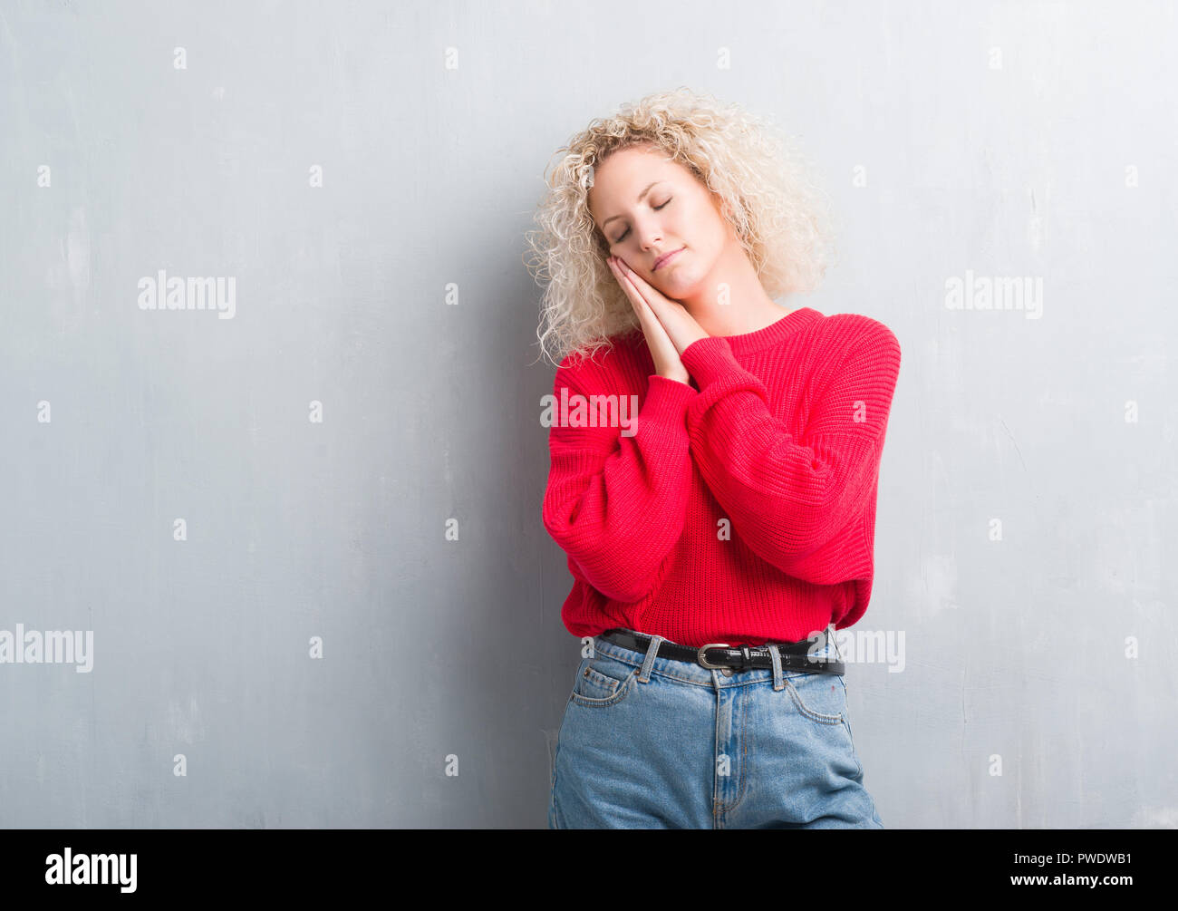 Young blonde woman with curly hair over grunge grey background sleeping ...