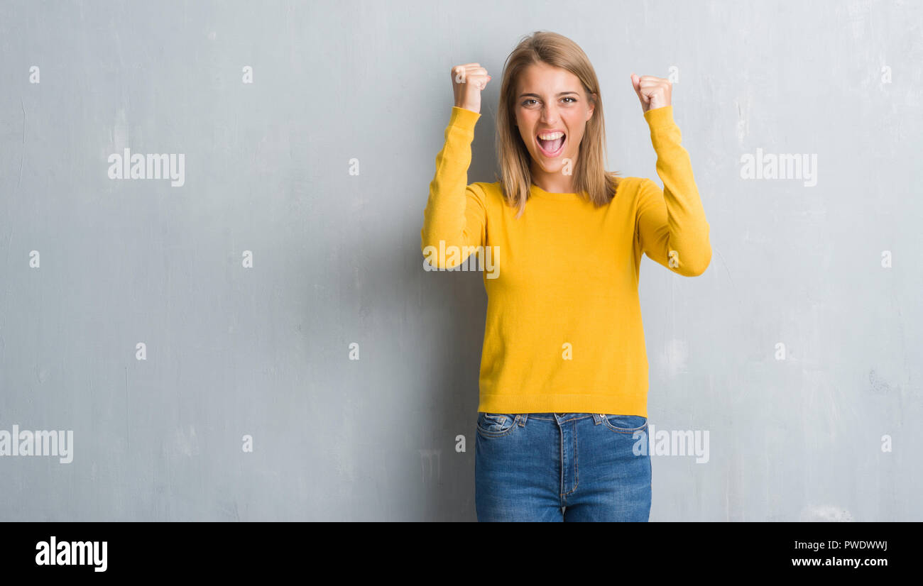 Beautiful young woman standing over grunge grey wall angry and mad ...