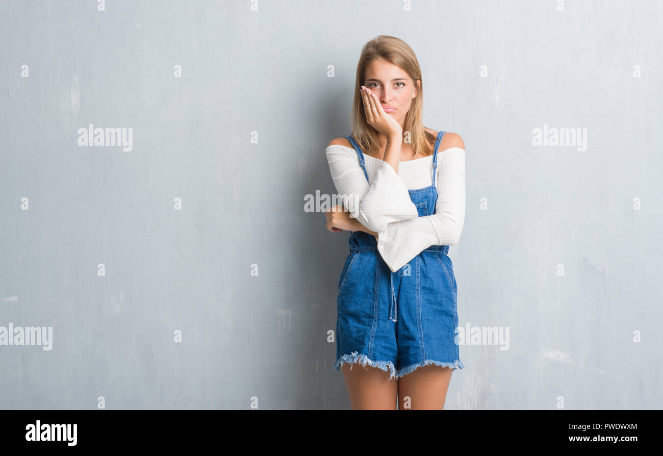 Beautiful young woman standing over grunge grey wall thinking looking ...