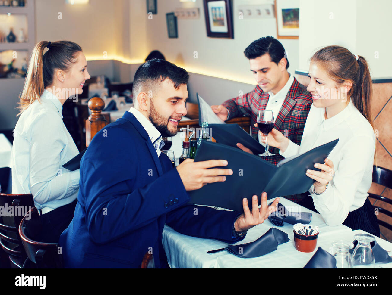 Group of smiling friends enjoying dinner at restaurant, choosing meal ...