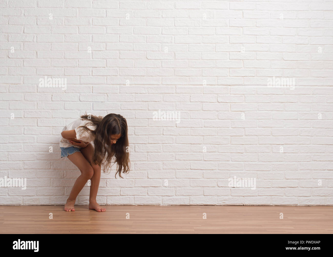 Young hispanic kid stading over white brick wall with hand on stomach ...