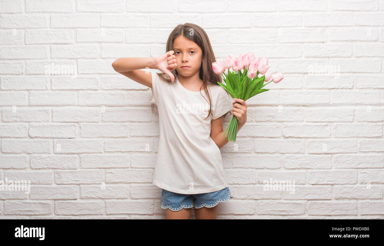 Young hispanic kid over white brick wall holding flowers on mother day ...