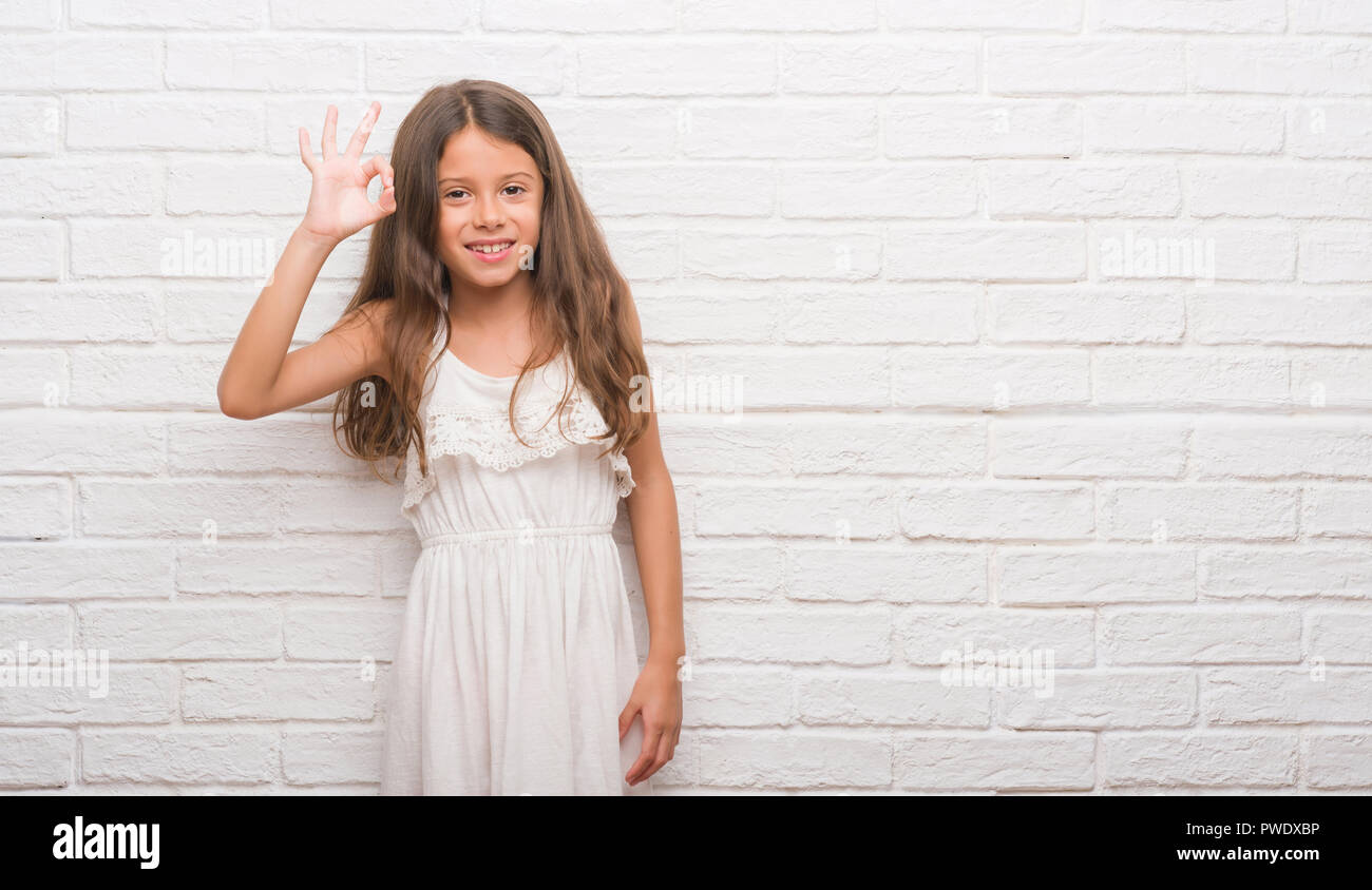 Young hispanic kid over white brick wall smiling positive doing ok sign ...