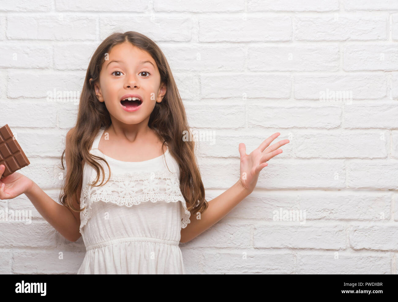 Young hispanic kid over white brick wall eating chocolate bar very ...