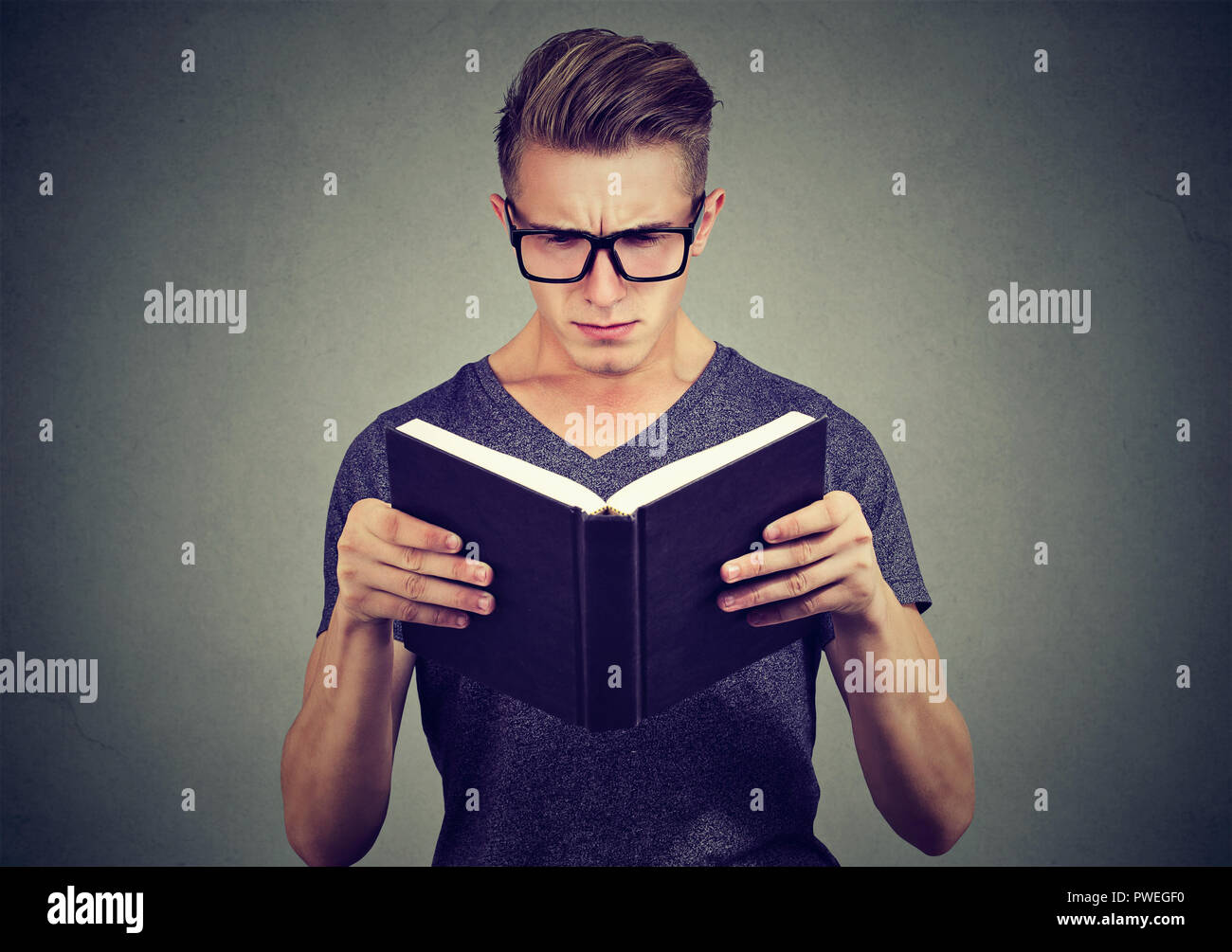 Young man in glasses looking confused while trying to read smart book ...