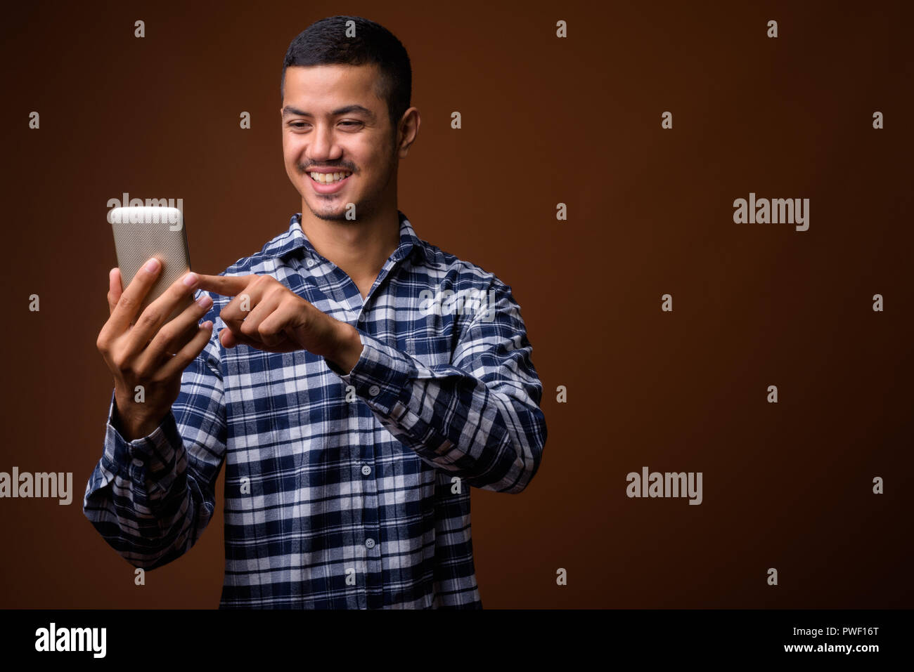 Young multi-ethnic Asian man against brown background Stock Photo - Alamy