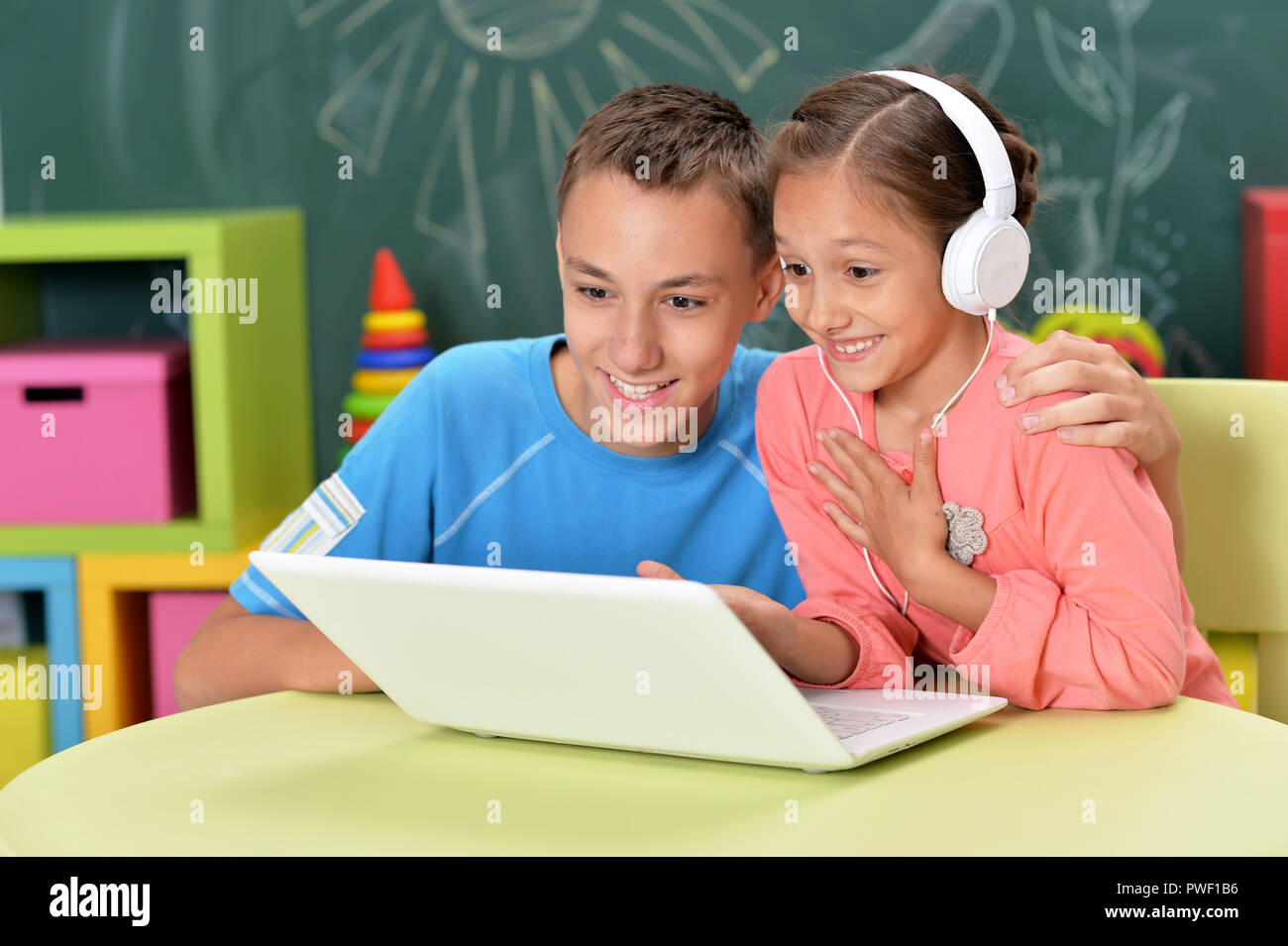 brother and sister using laptop white sitting at table, girl wearing ...