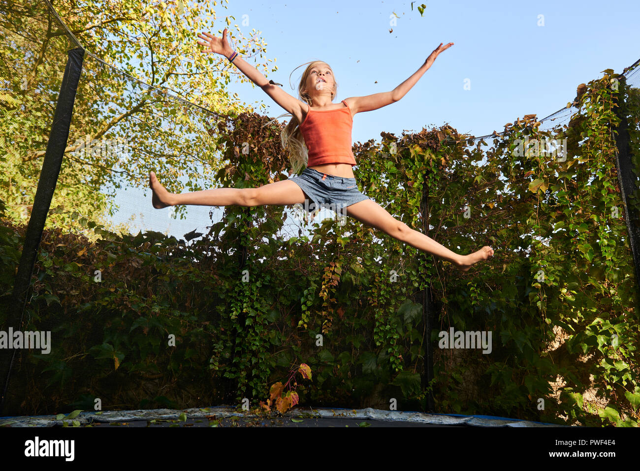 Child cute blond girl playing and jumping on trampoline with greenery ...