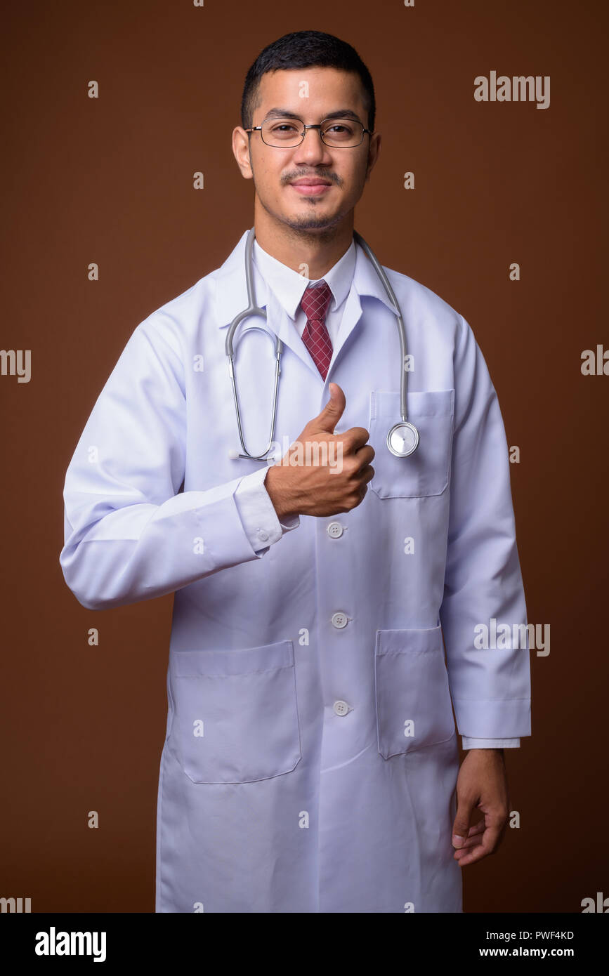 Young multi-ethnic Asian man doctor against brown background Stock ...