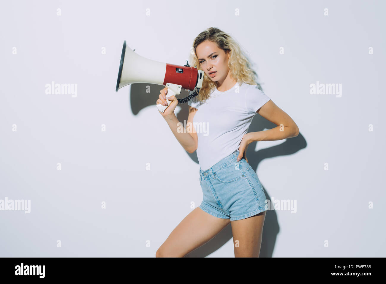 Blonde woman shouting with a megaphone isolated on a white background ...