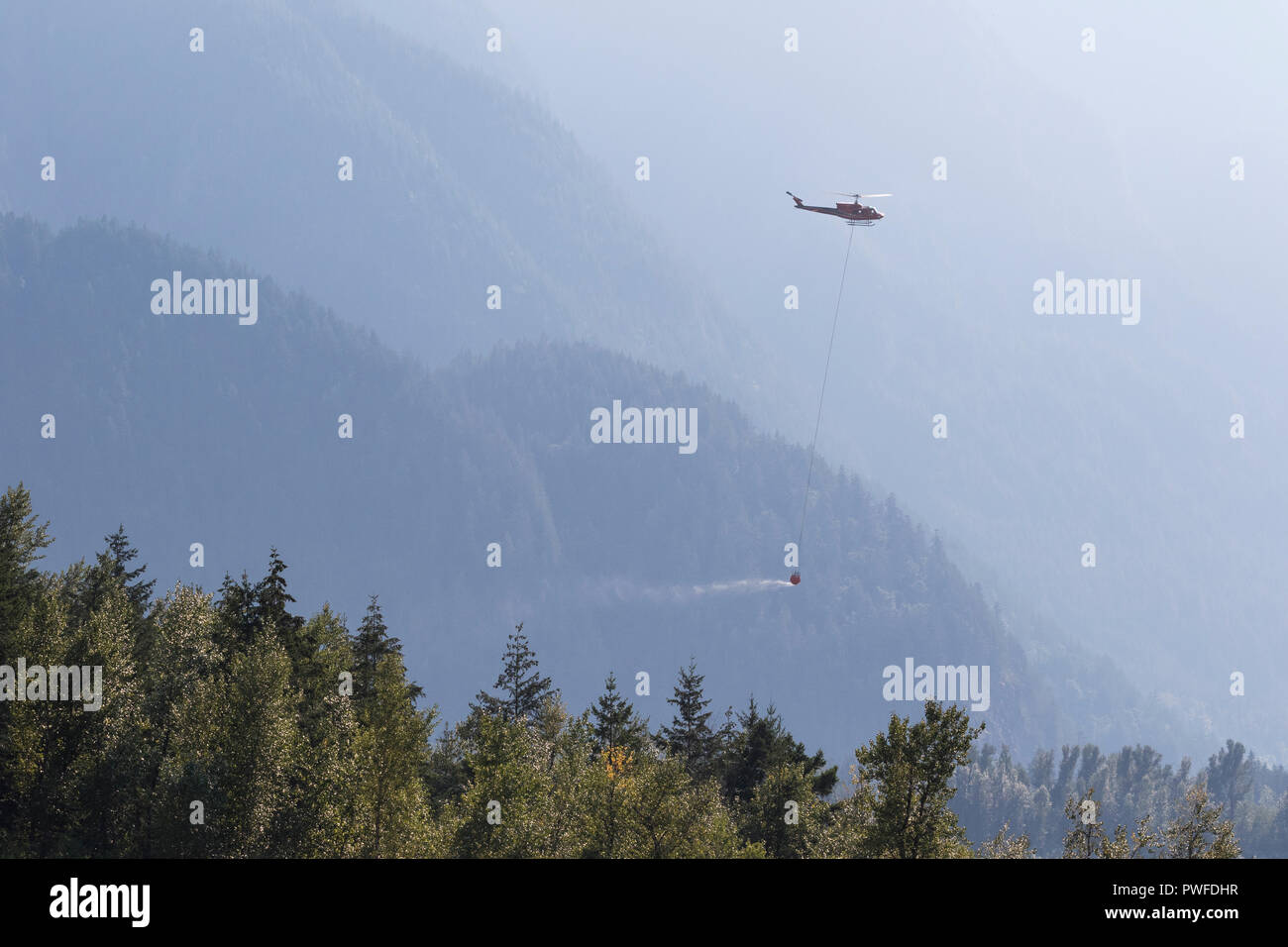 Helicopter carrying water to extinguish forest fire, British Columbia ...