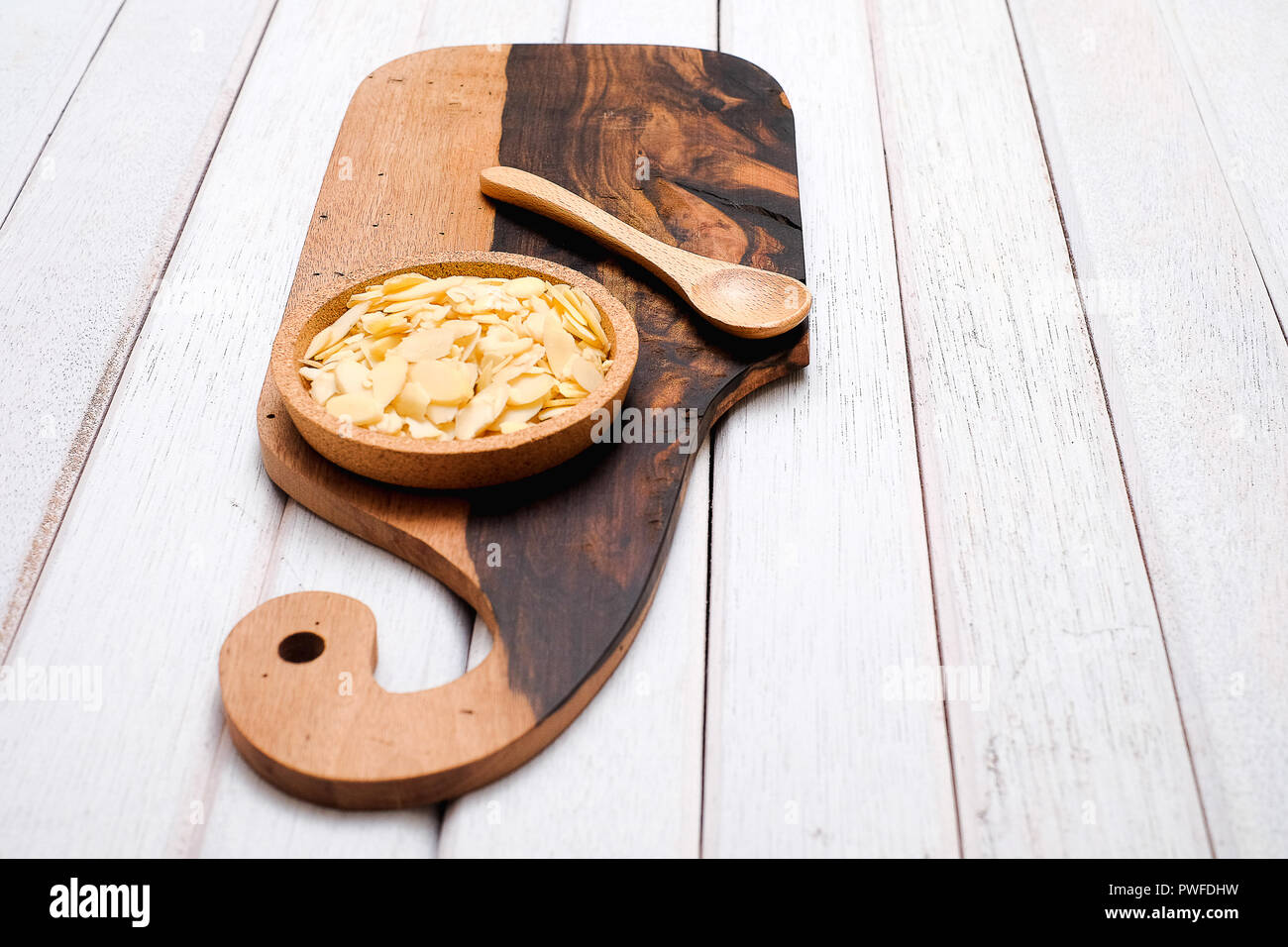 Sliced almond nuts in a wooden bowl and wooden spoon with cutting board ...