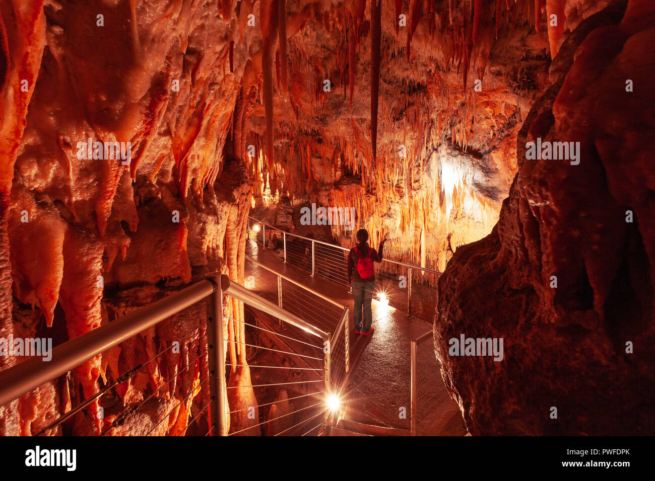 Tourist pointing a flashlight at stalactites in limestone cave in ...