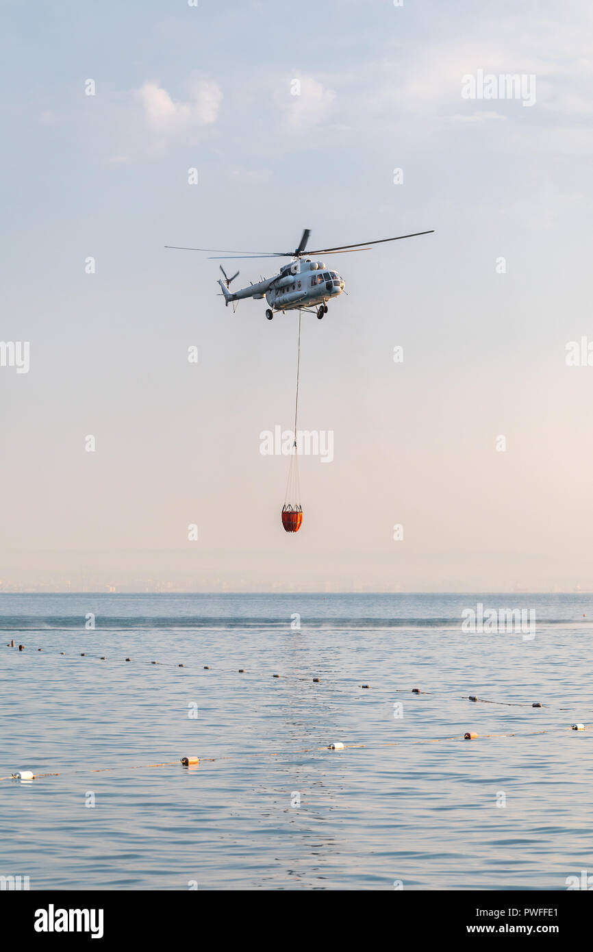 A helicopter with a red basket is lowered over the sea to catch water ...