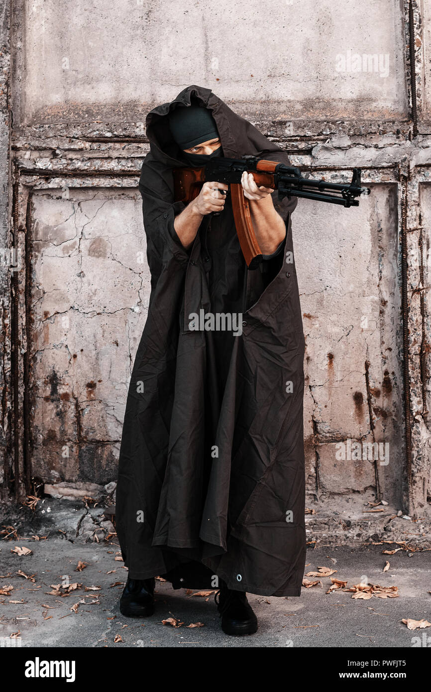 a man in a military coat and a balaclava aiming with Kalashnikov RPK ...