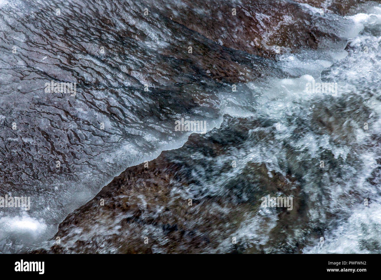 The detailed look at water runs under ice in a river. The snow is ...