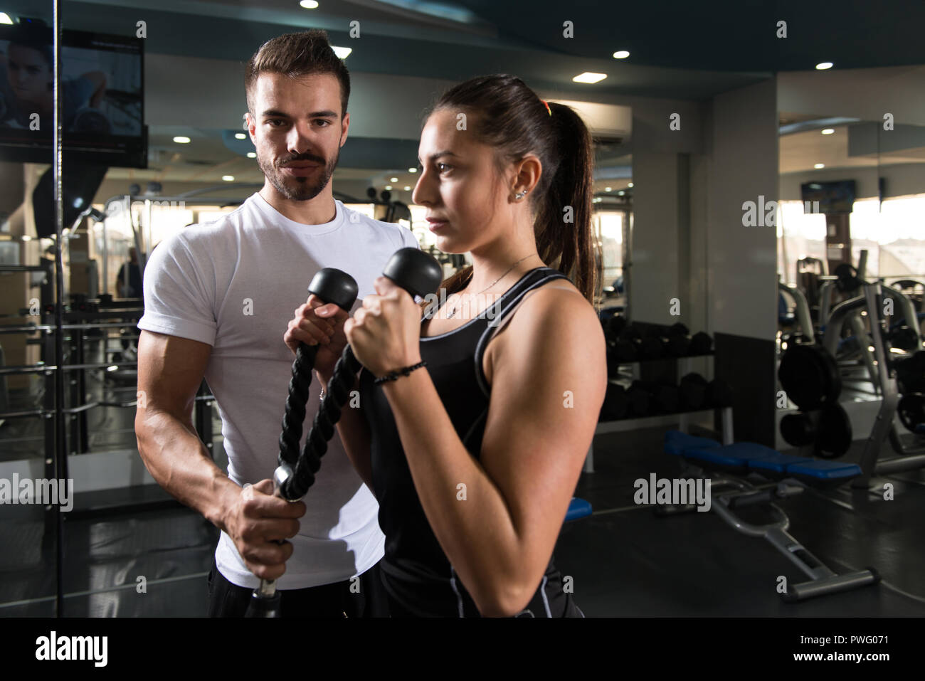 Personal Trainer Showing Young Woman How To Train Biceps In The Gym ...