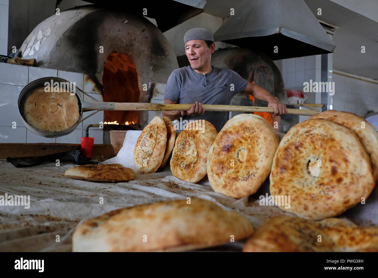 An Uzbek baking Naan oven-baked flatbread in Chorsu Bazaar also called ...