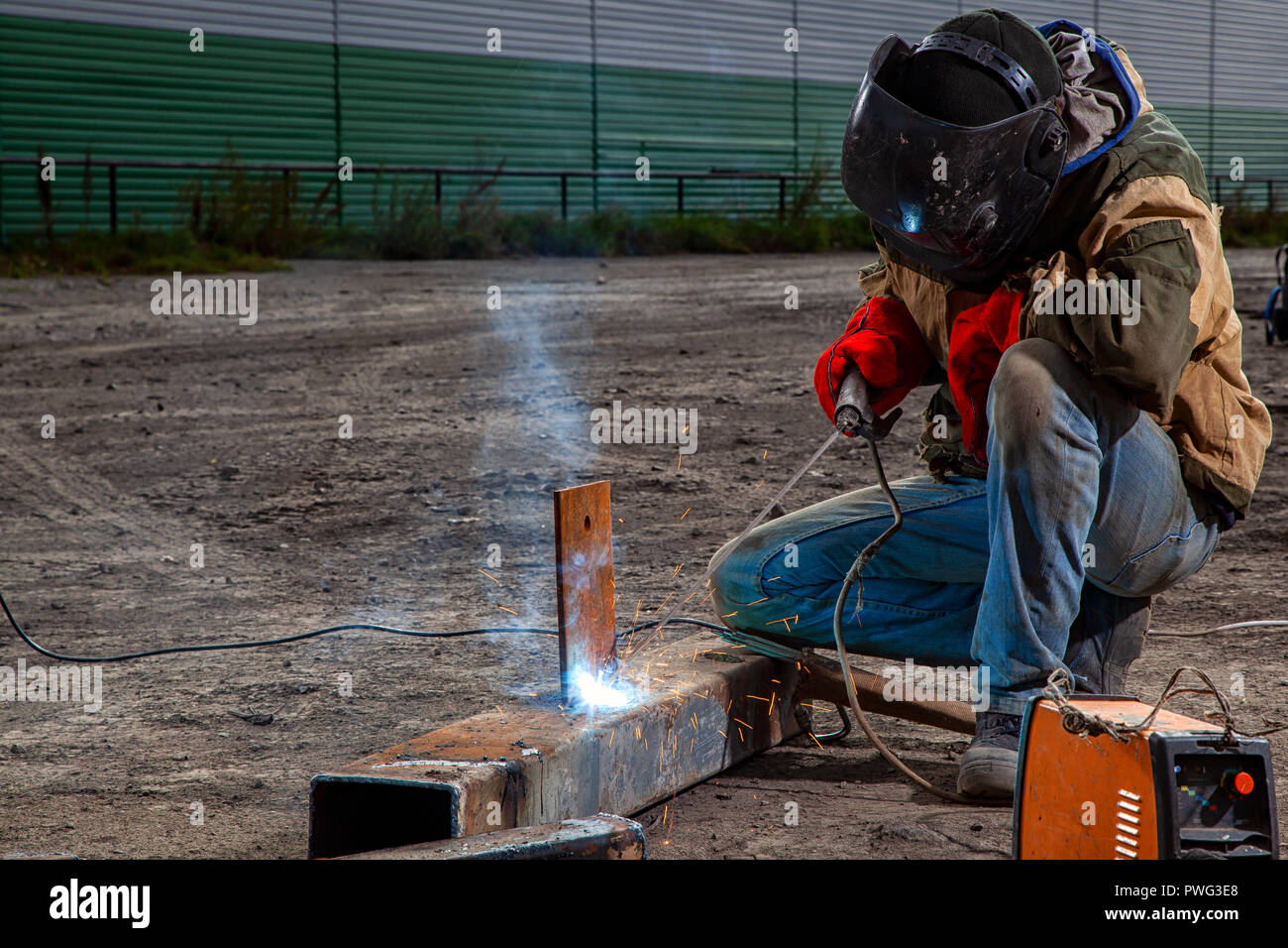 Man welder in welding mask, building uniform and red protective gloves ...