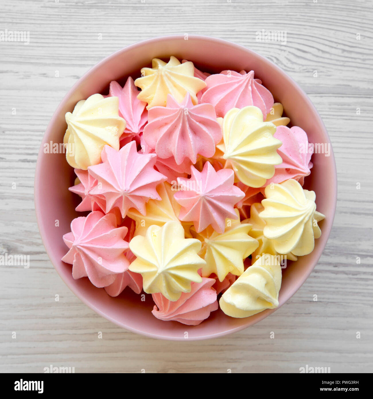 Mini meringues in a pink bowl over white wooden surface, view from ...