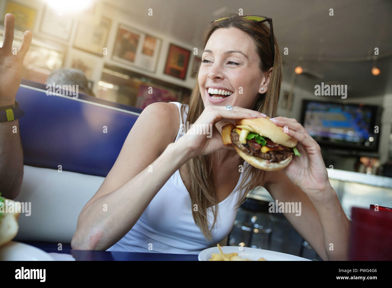 Portrait of cheerful girl eating hamburger in fast food restaurant ...