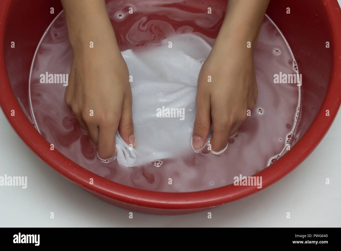 The girl erases a children's white T-shirt in a red basin from stains ...