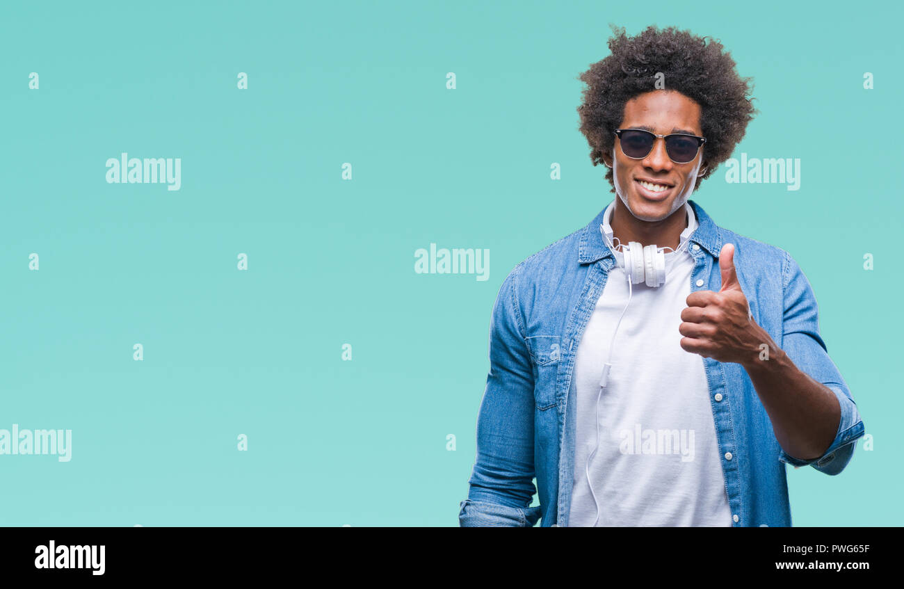 Afro american man wearing headphones listening to music over isolated background doing happy ...