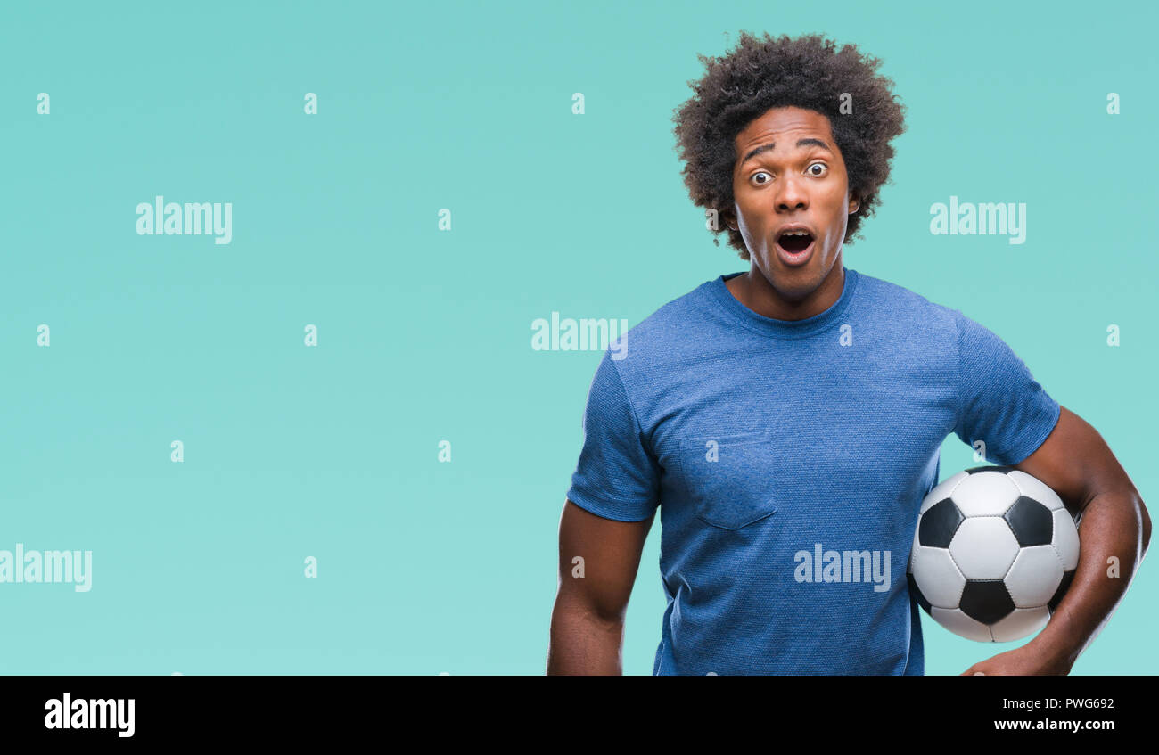 Afro american man holding football ball over isolated background scared ...