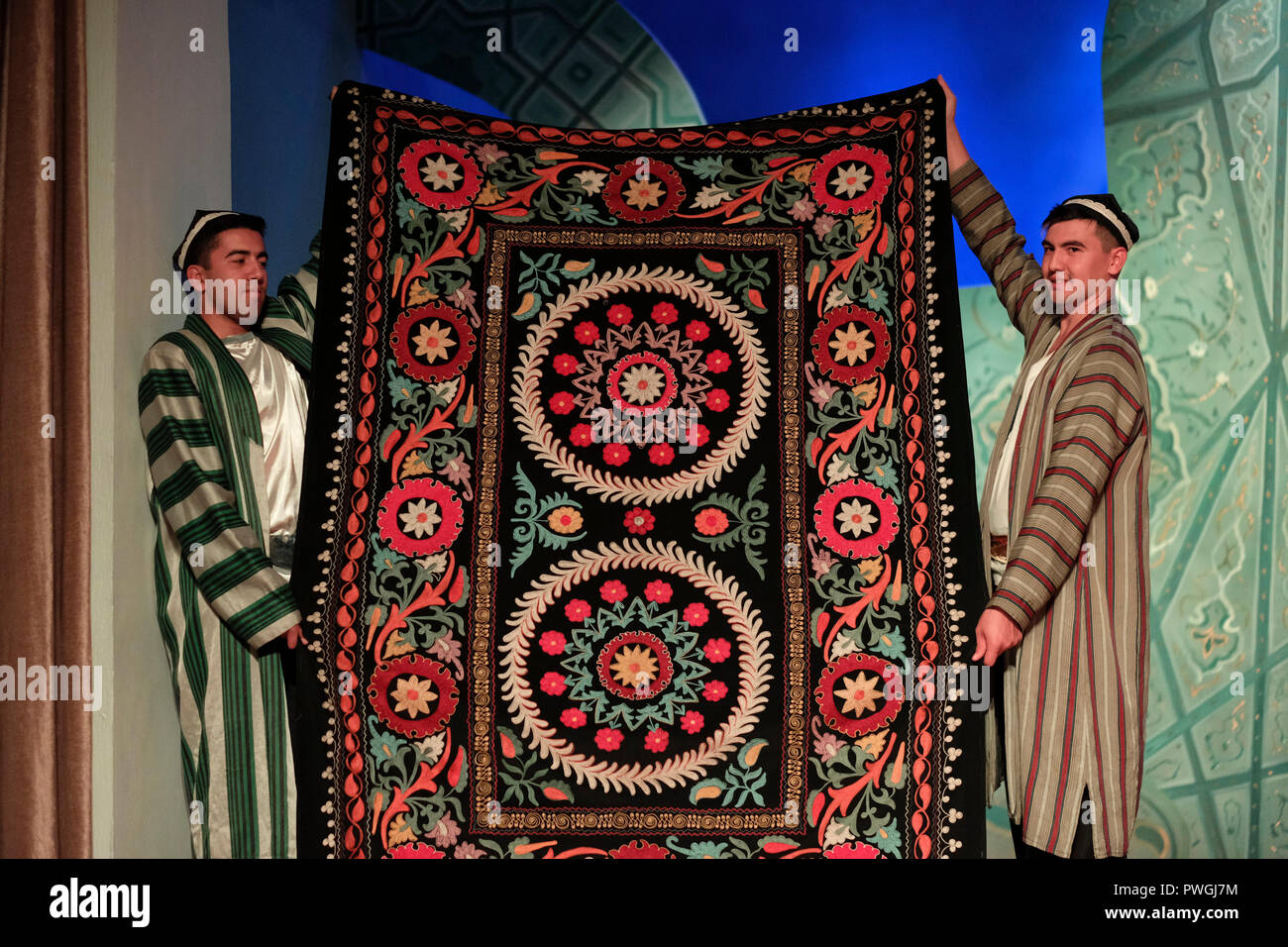 Dancers wearing traditional garment hold a handmade Uzbek rug during an ...