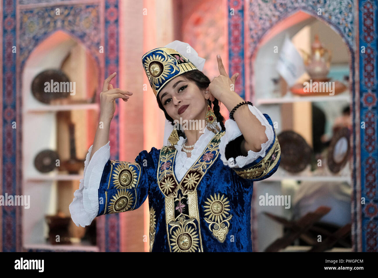 Young Uzbek woman wearing traditional satin fabric richly embroidered with golden thread dancing ...