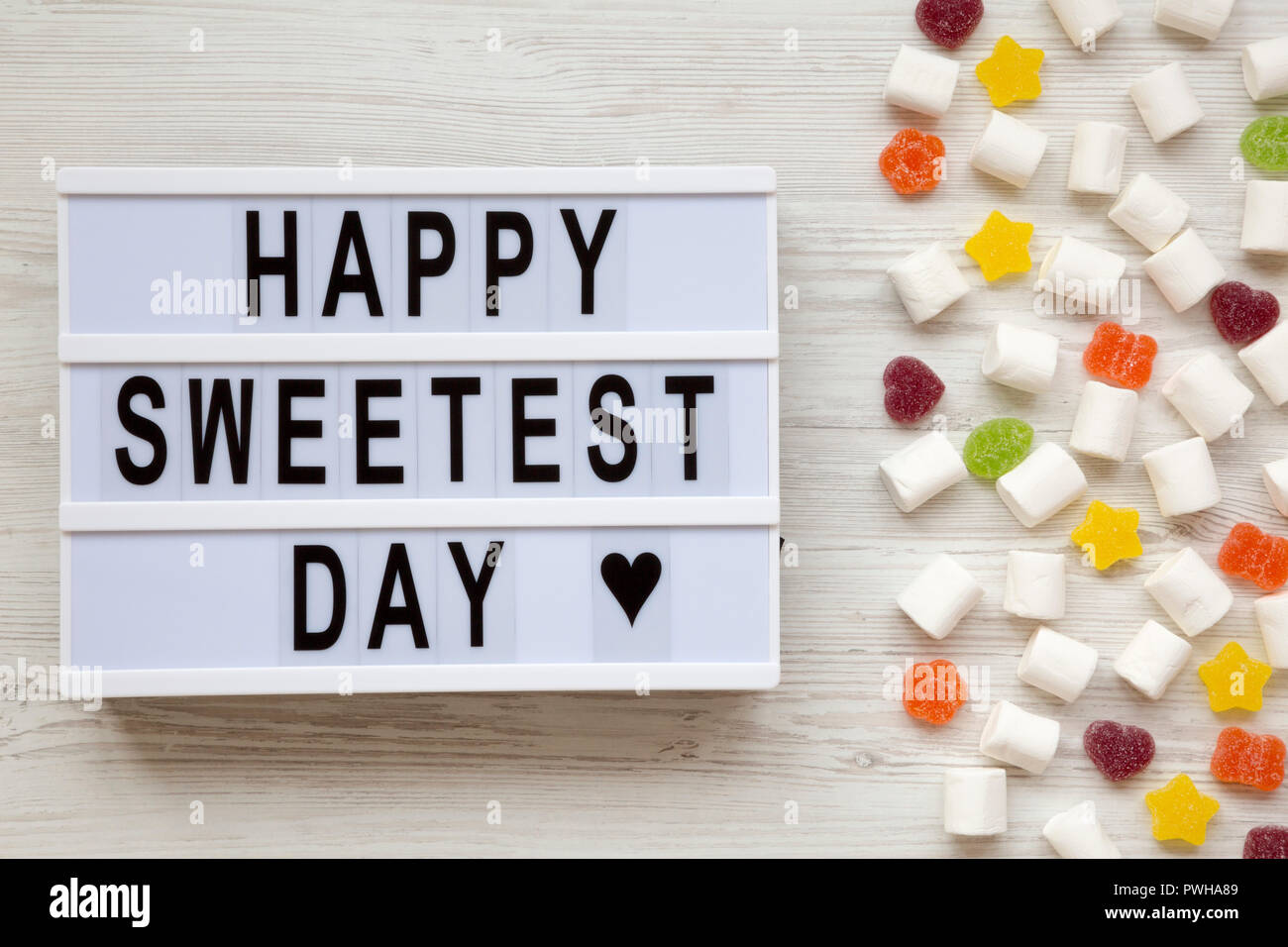 Modern board with 'Happy Sweetest Day' word and candy on a white wooden ...