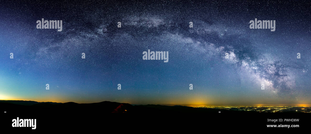 Panoramic shot of Milky Way's galactic arc over city lights Stock Photo ...