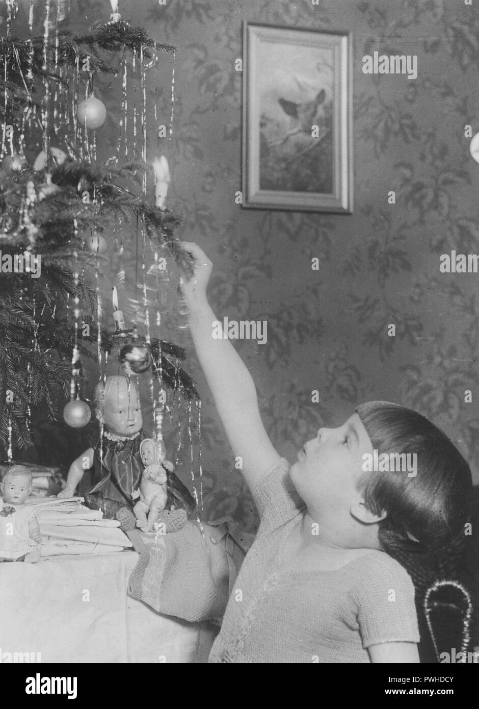 Christmas in the 1920s. A girl is decorating the christmas tree and is ...