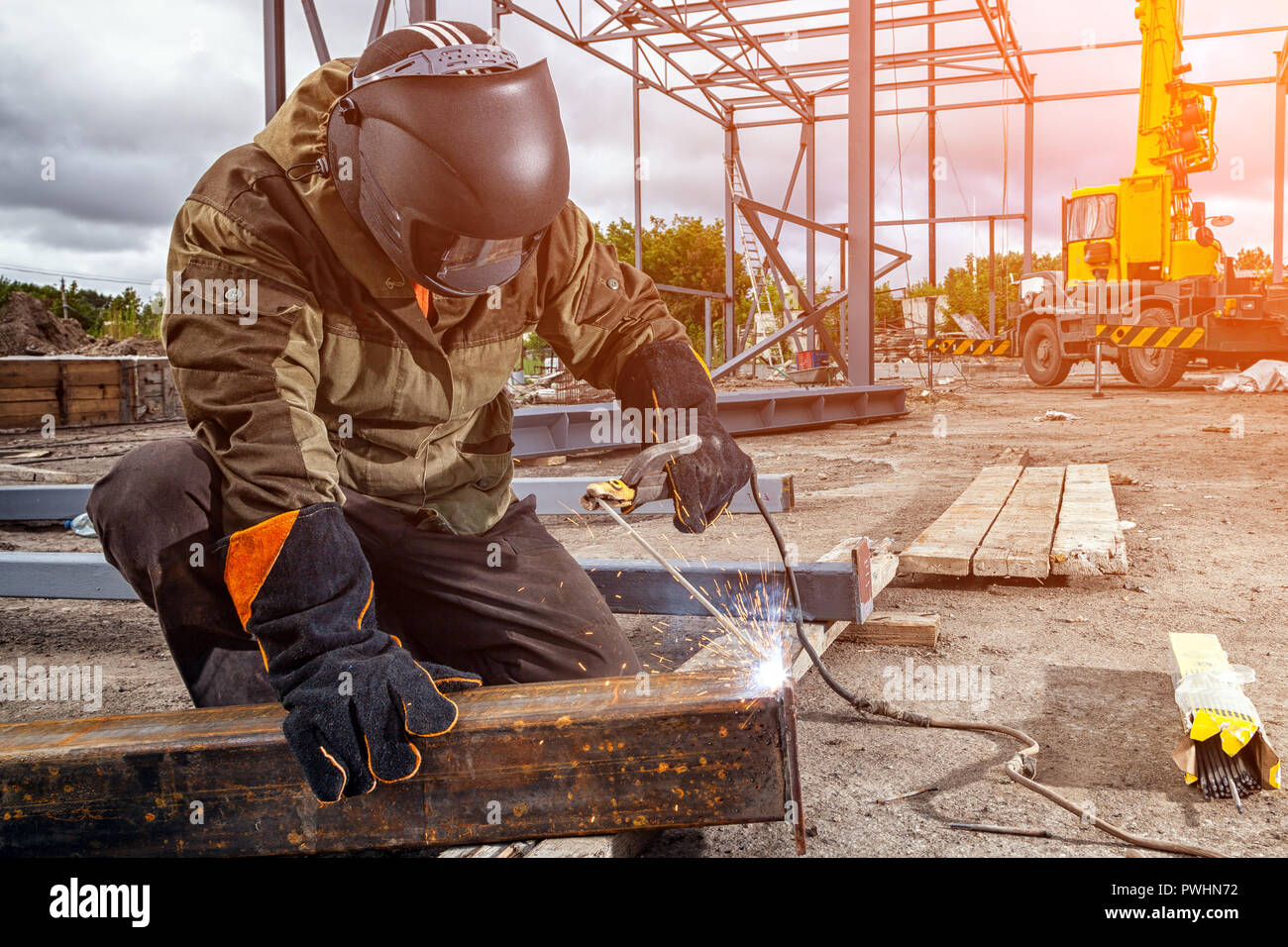 A strong man is a welder in brown uniform, welding mask and welders ...