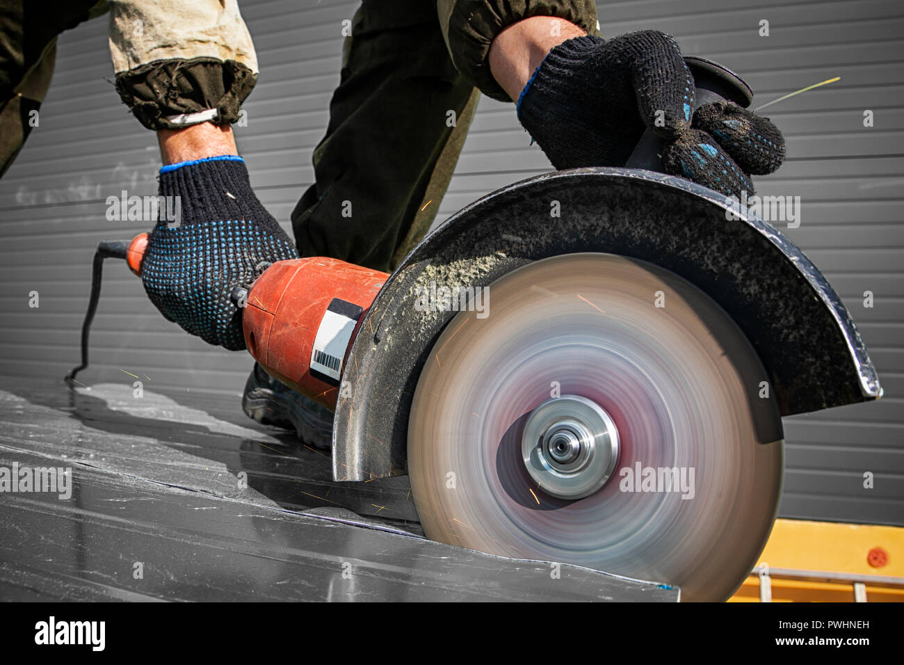 A young male builder in working clothes and black gloves grinds a metal ...