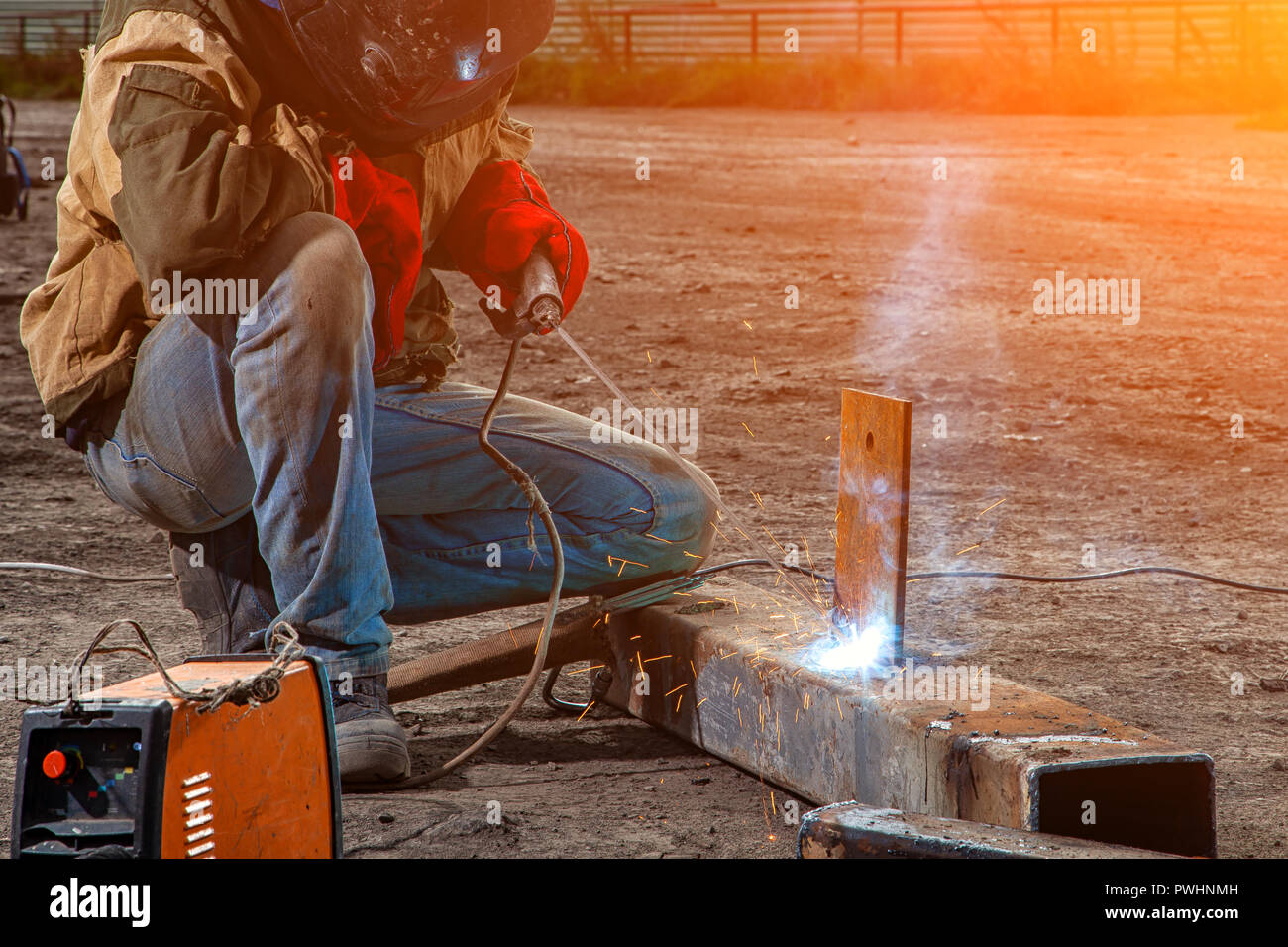 Man welder in welding mask, building uniform and red protective gloves ...