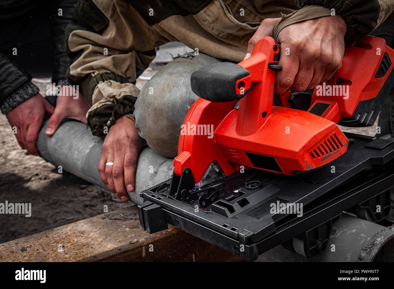 Close-up of a man builder sawing metal with a hand modern red circular ...