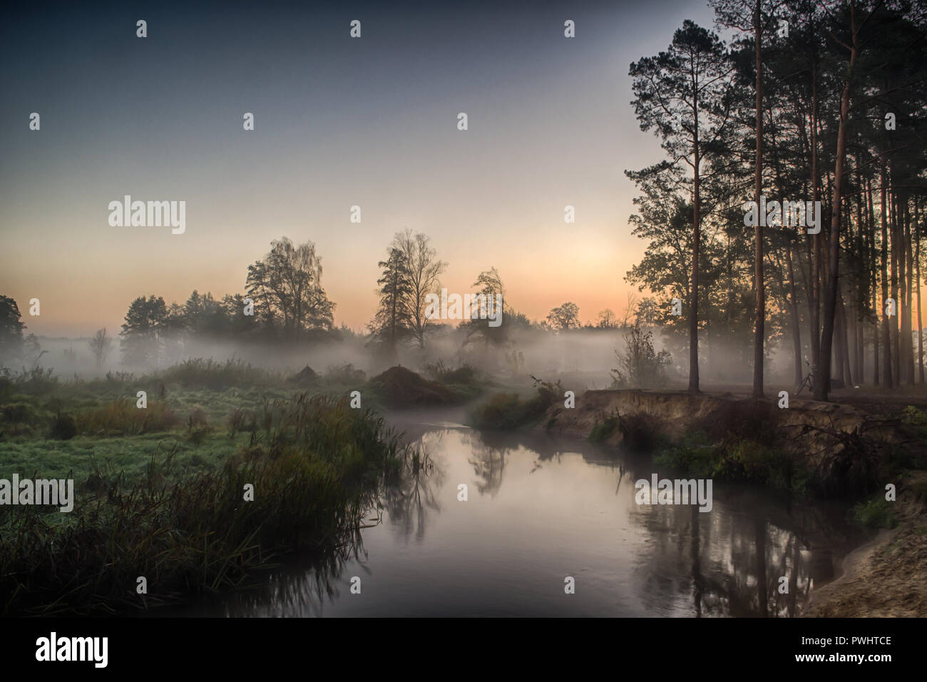 River in the fog, just before sunrise. A warm glow in the clouds from ...