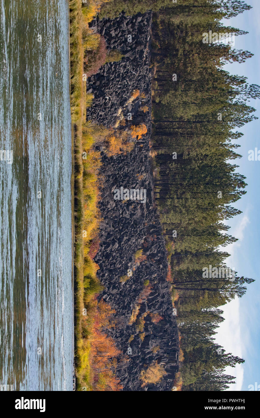 A talus slope gives way to bright fall foliage on the bank of the ...