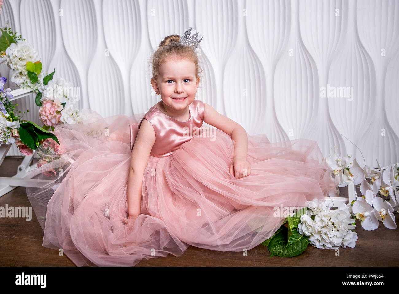 The little princess in a beautiful pink dress sits on the floor near ...