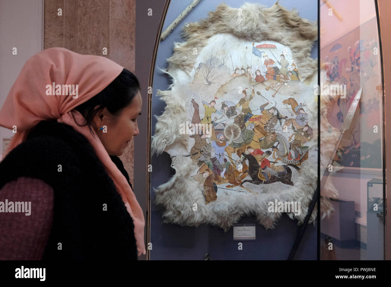 An Uzbek visitor views a painting on an animal skin showing battle ...